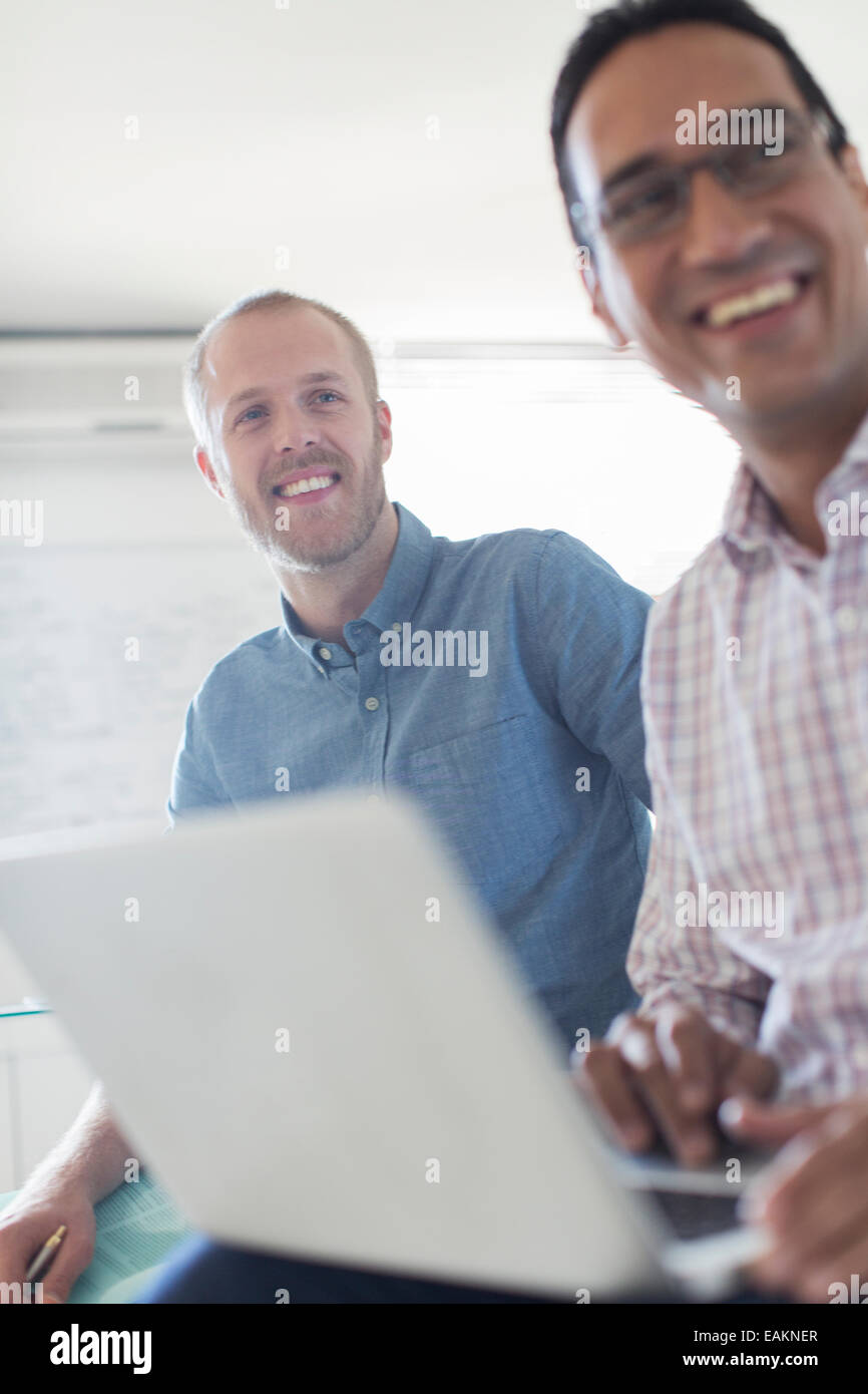 Two smiling businessmen using laptop in office Stock Photo - Alamy