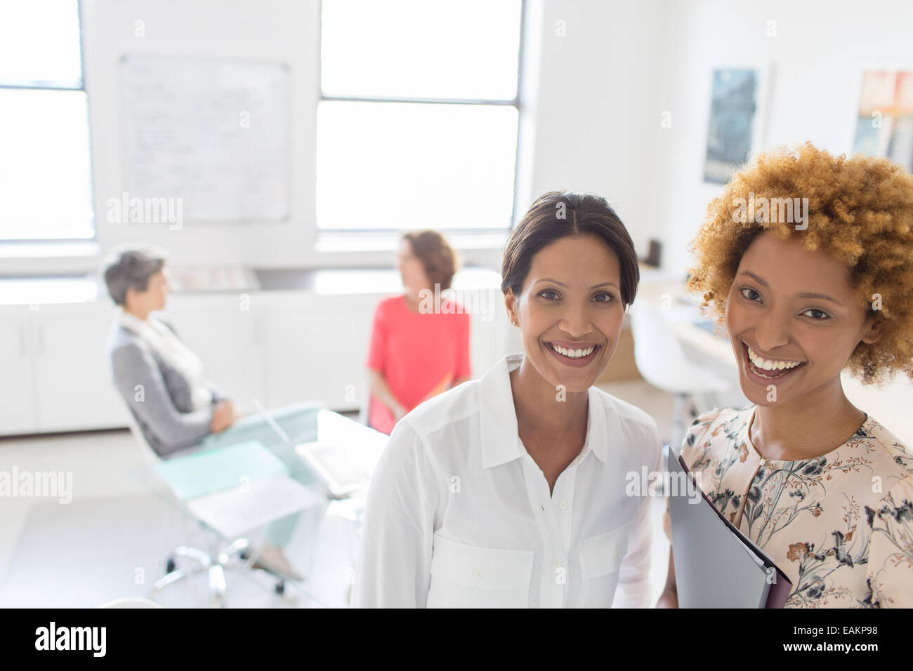 Portrait of two smiling business women in office, colleagues talking in ...
