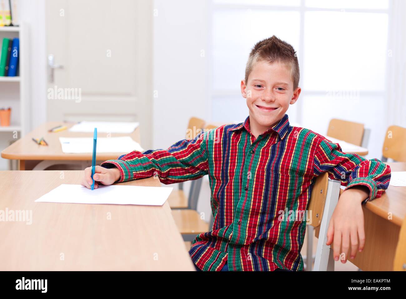 Confident boy in empty classroom, sitting alone at table Stock Photo ...