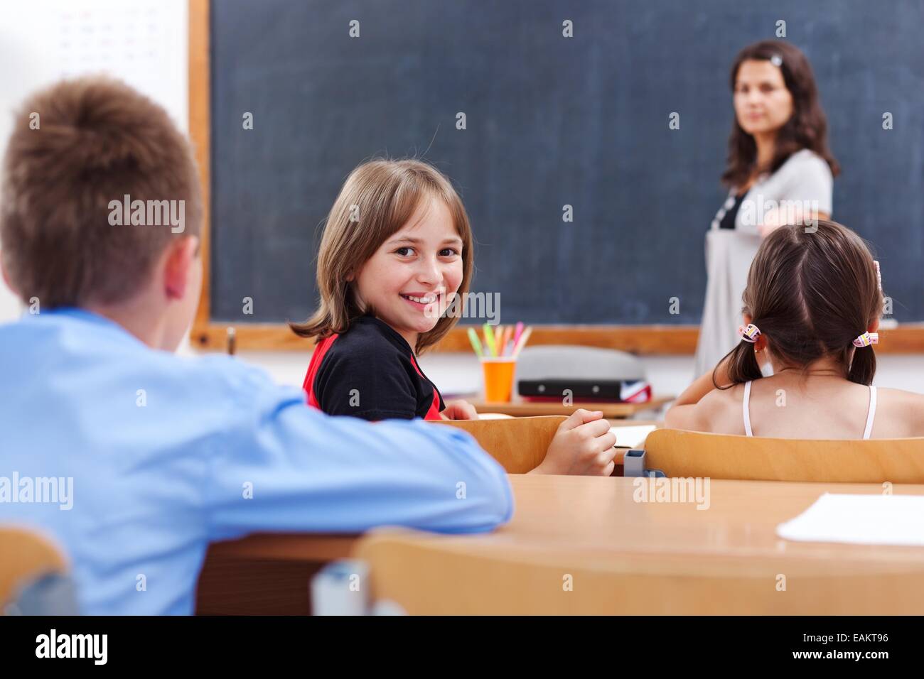 Cheerful school girl looking back in class room while the teacher ...