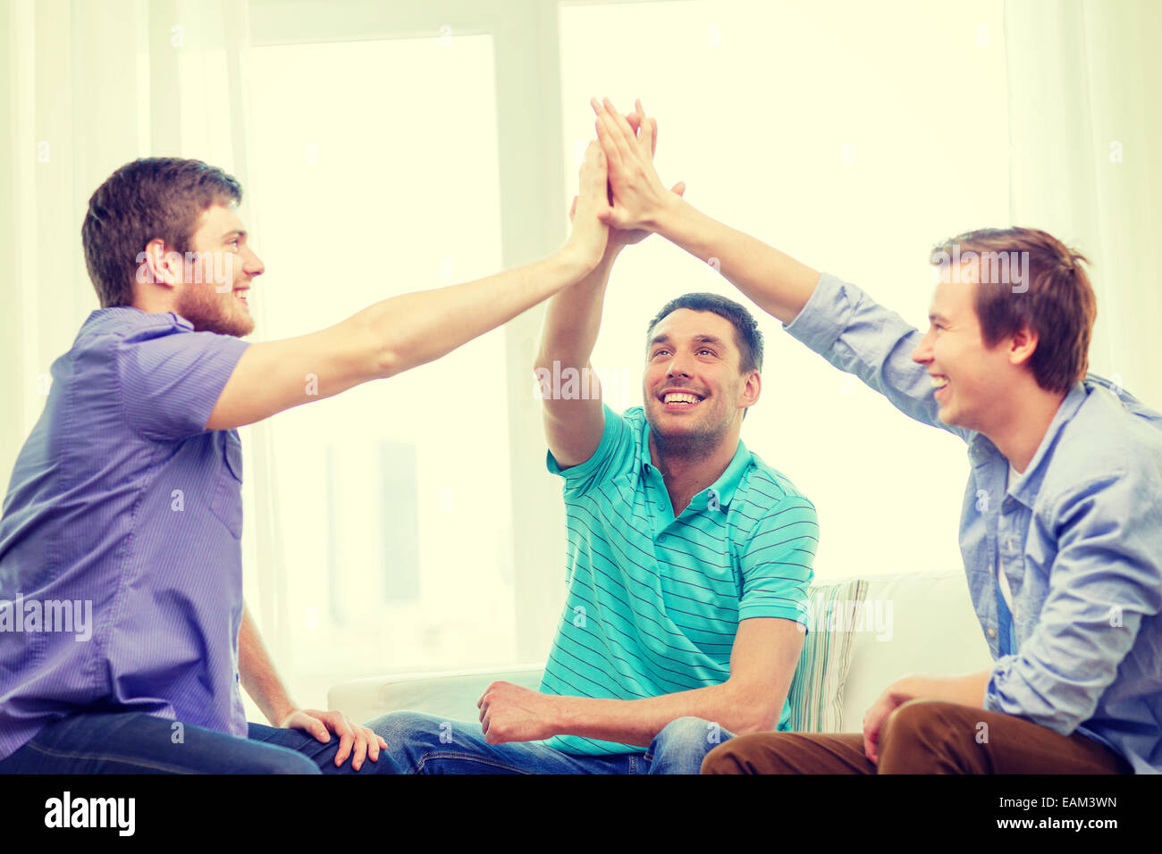 smiling male friends giving high five at home Stock Photo - Alamy