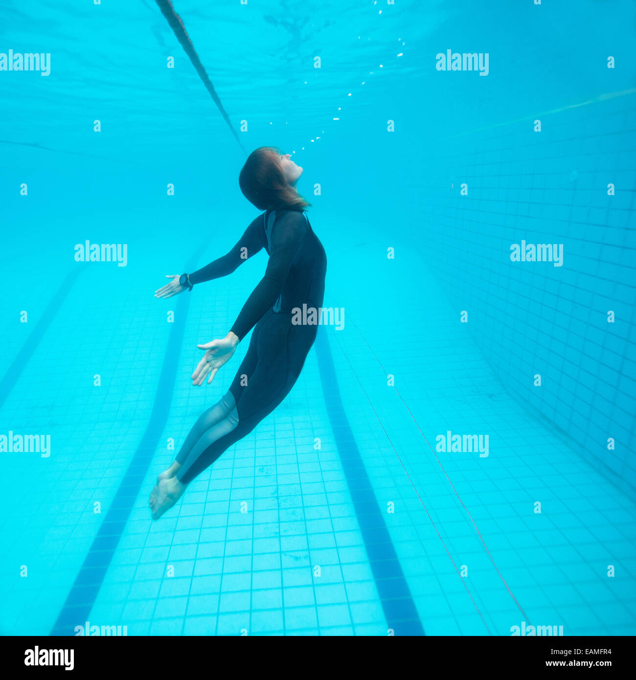 Female diver appearing to fly upwards while underwater in swimming pool ...