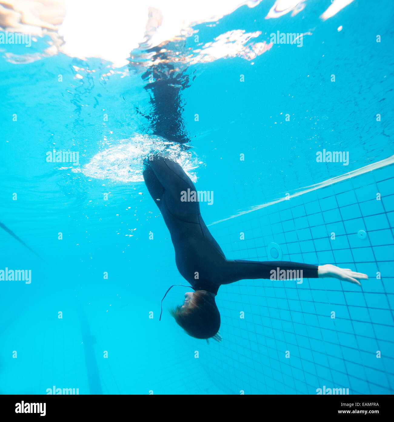 Female Diver Calmly Diving Downwards Through Surface Into Swimming Pool
