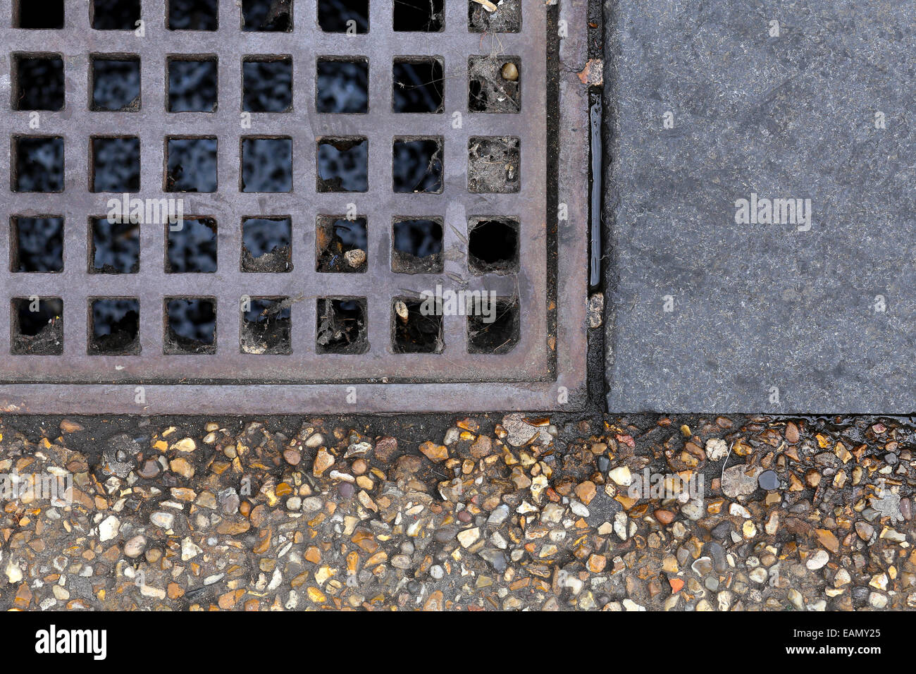 Metal grill drain cover in a pathway of asphalt and pavement grey stone ...