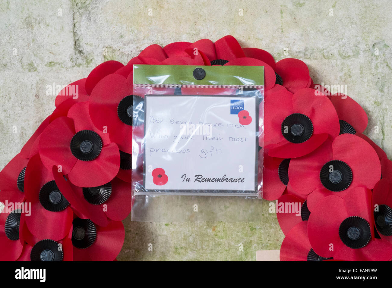 Poppy wreath leaning against stone wall with British Legion note of ...