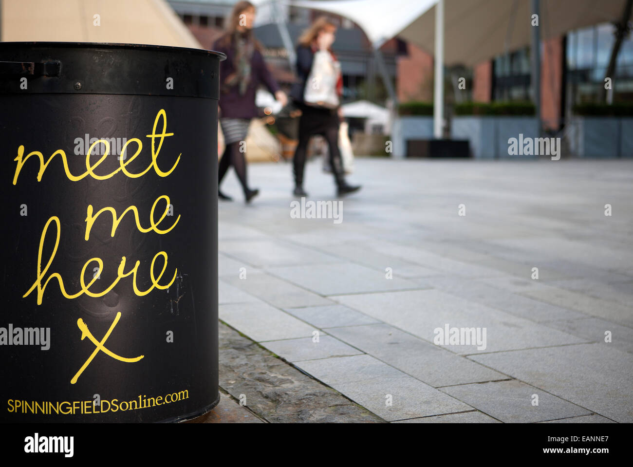 'Meet Me Here' sign on side of garbage bin with two blurred female ...