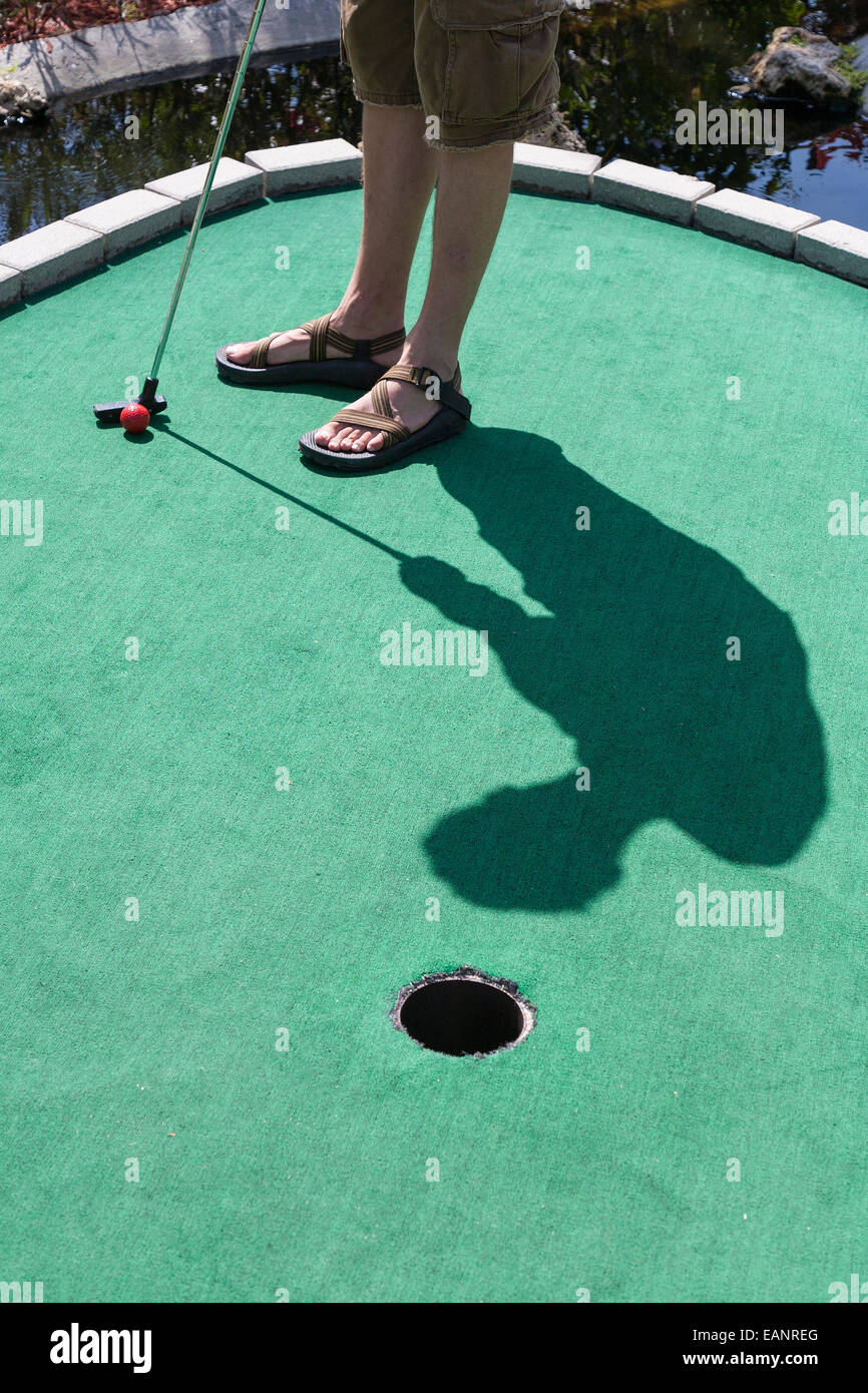 Shadow of mini golf player points to the hole he putts for on green ...