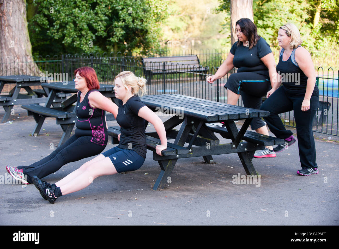 Four overweight women on a boot camp doing exercises on a park picnic ...