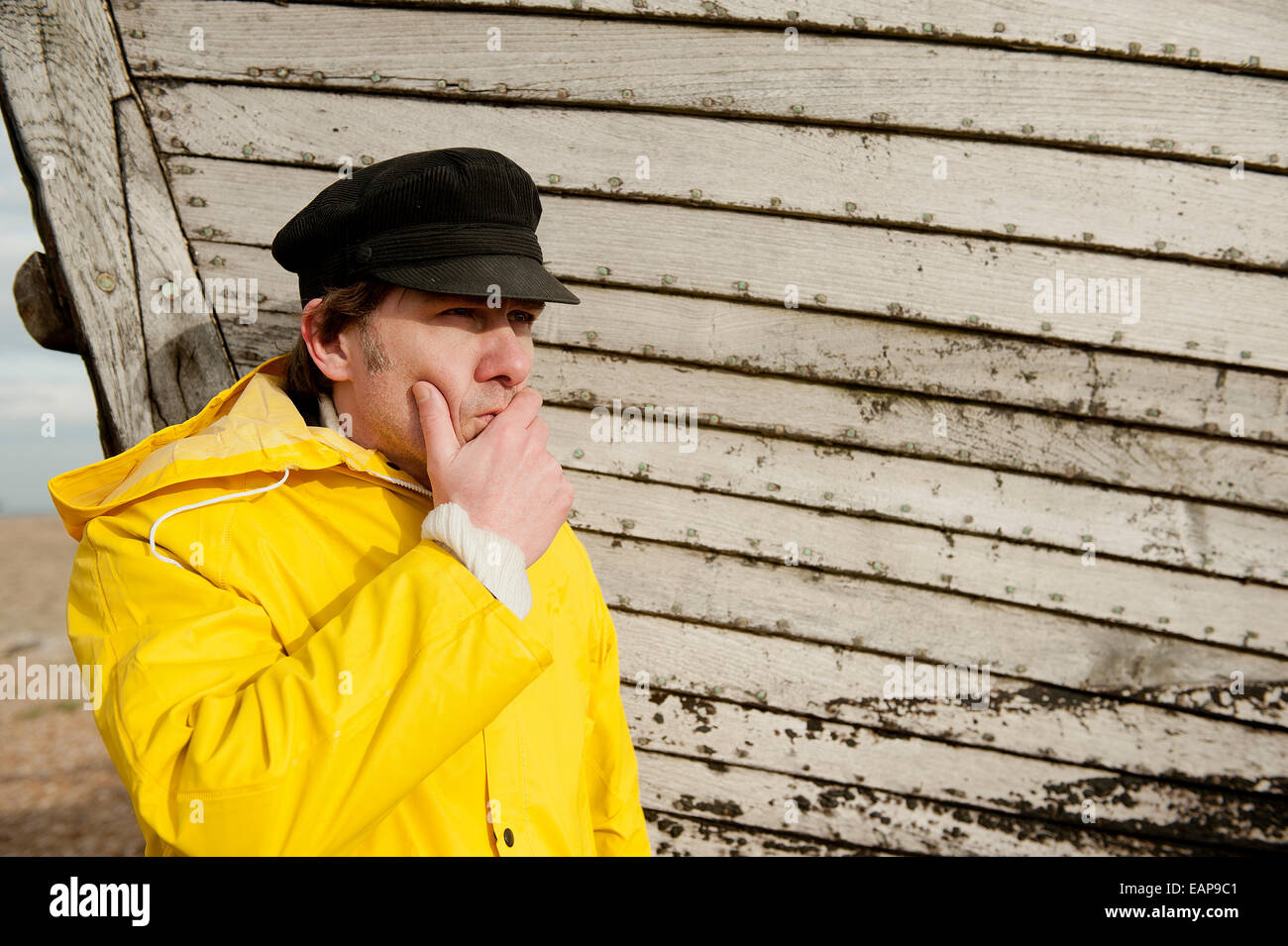 Pensive fisherman in yellow waterproof overalls, standing beside an old ...