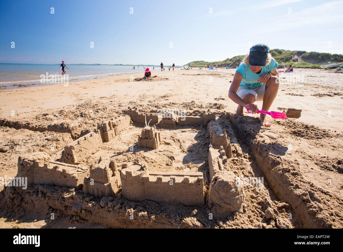 A woman building a sandcastle on Bamburgh Beach, Northumberland, UK ...