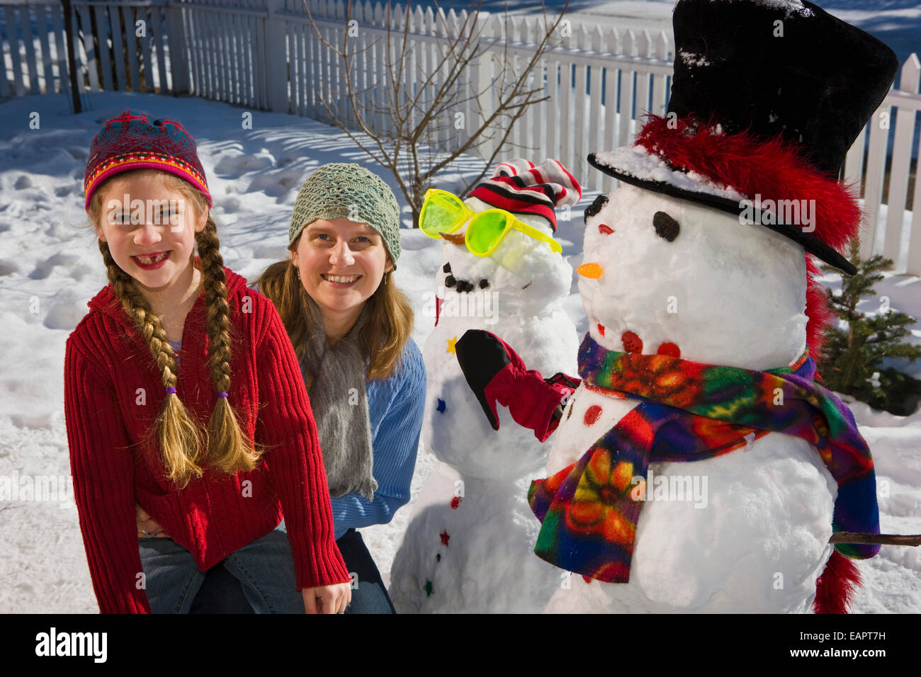 Mother Helping Daughter Decorate A Snowman In The Front Yard Of An ...