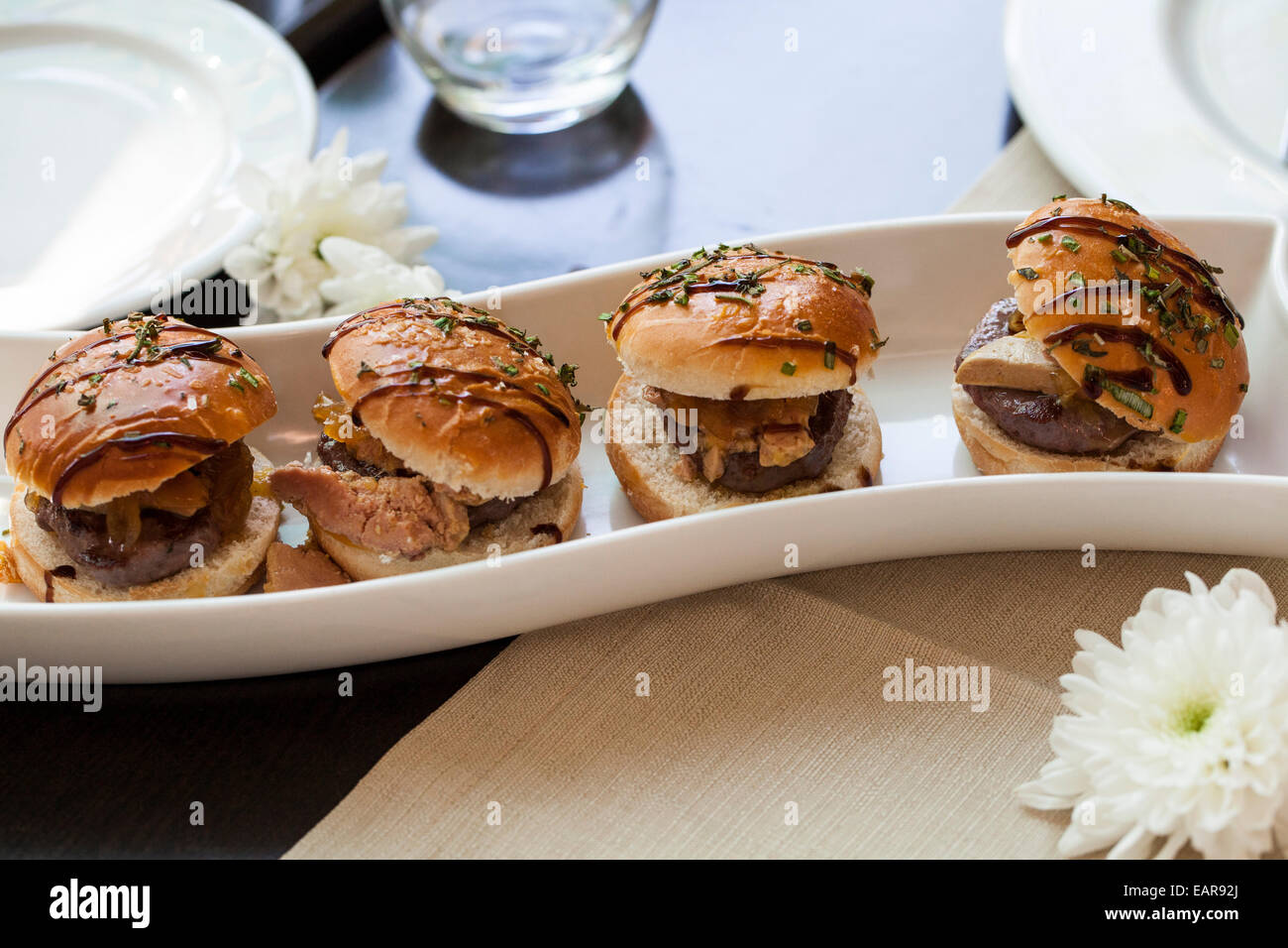 Mini beef burgers on rolls on a curved platter on a restaurant table ...