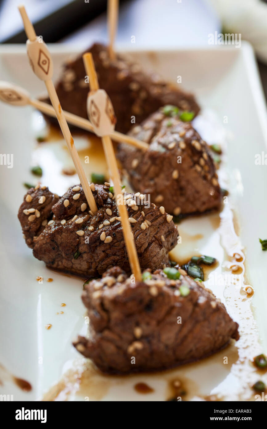 Small beef steaks with sesame seeds and a sauce on small cocktail ...