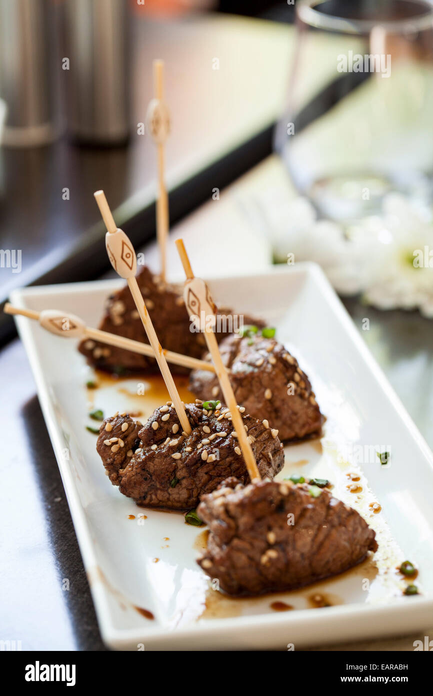 Small beef steaks with sesame seeds and a sauce on small cocktail ...