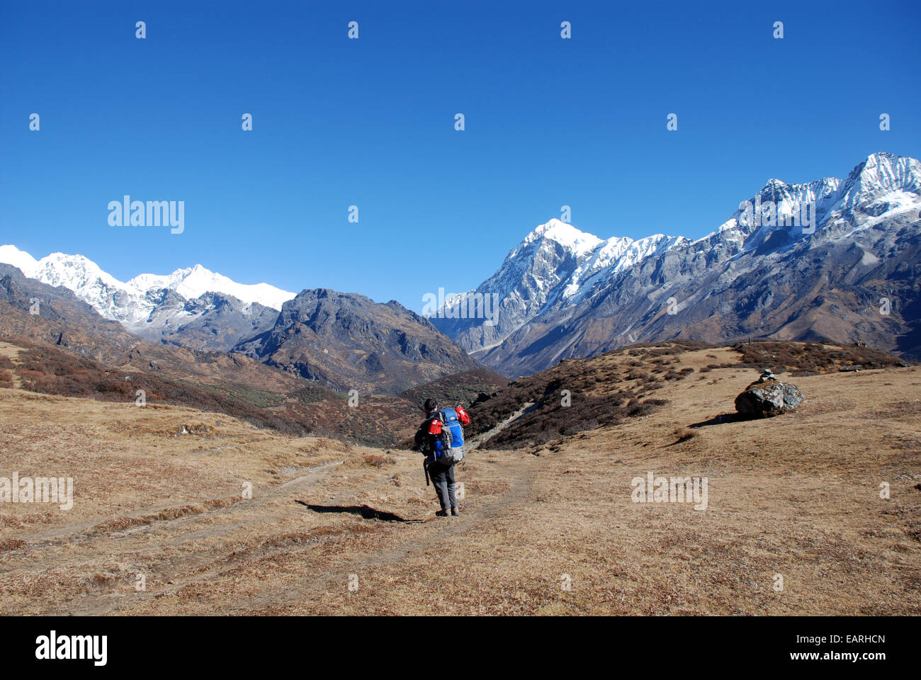 A trekker carrying a heavy rucksack walks on a high path towards the ...