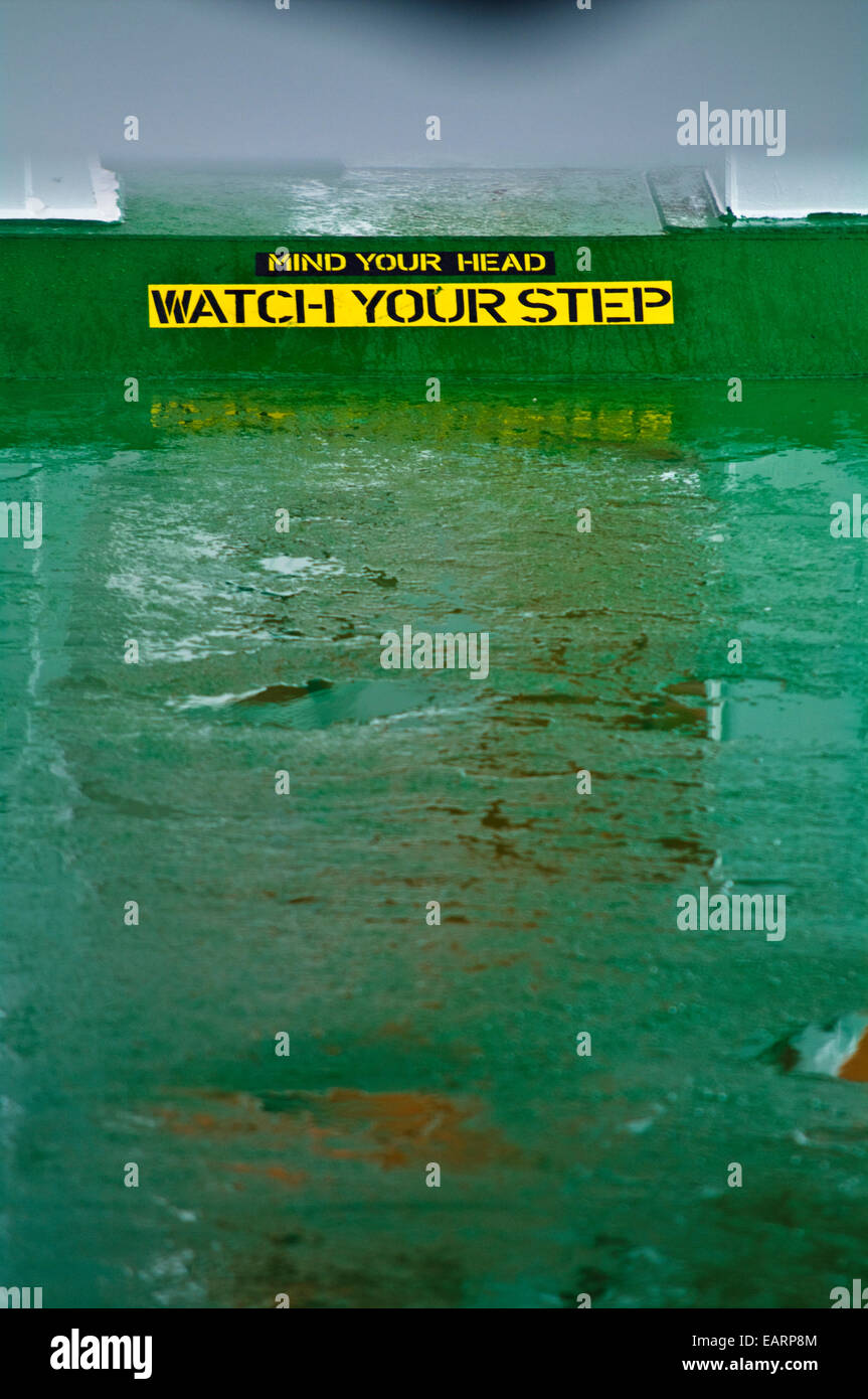 A sign warns about a low ceiling and hidden step on a wet ship deck ...