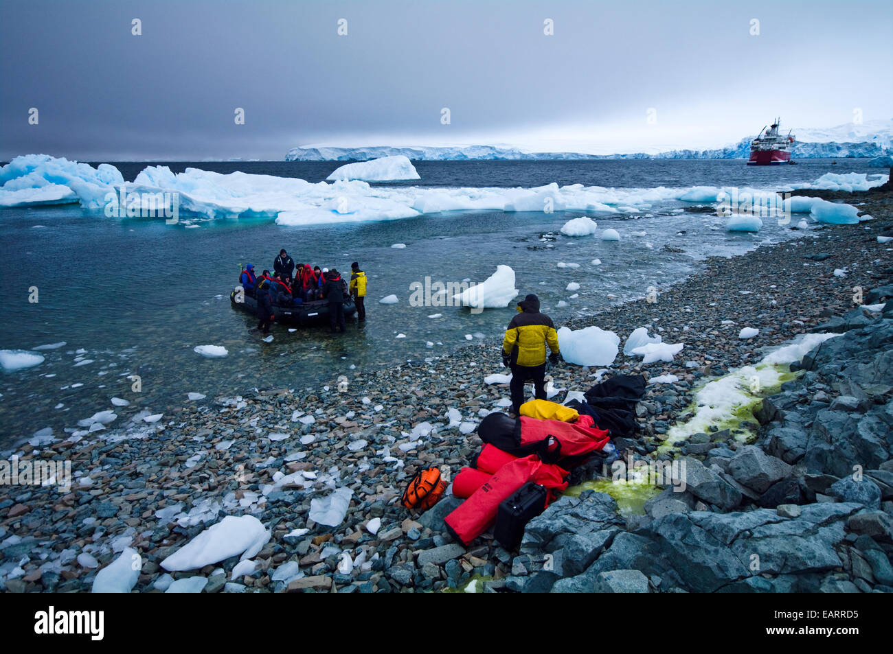 Tourists disembark from a zodiac boat to explore an icy rugged island ...