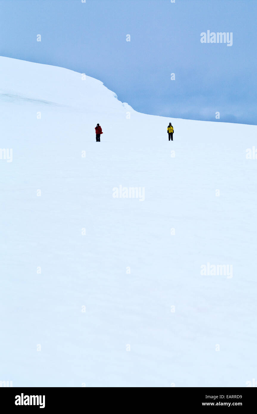 A tourist and guide explore a barren ice slope on a rugged island Stock ...