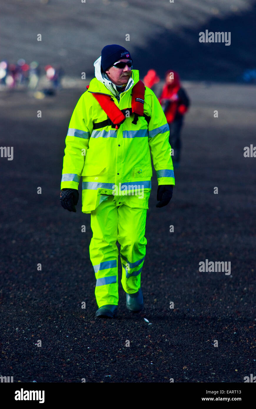 A tourist in fluorescent alpine clothing hiking on a volcanic beach ...