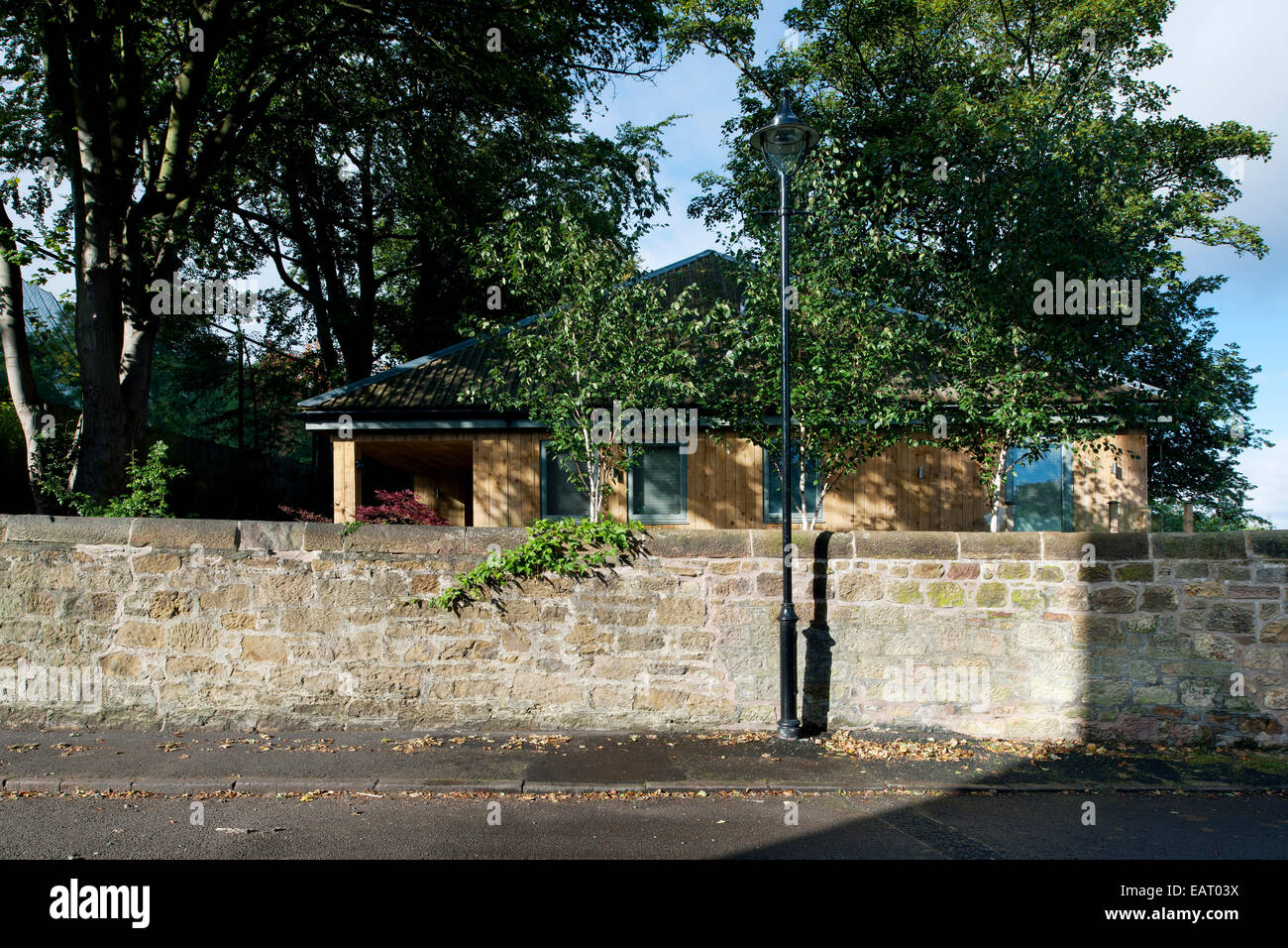Timber bungalow in woodland setting seen beyond stone wall, Midlothian ...