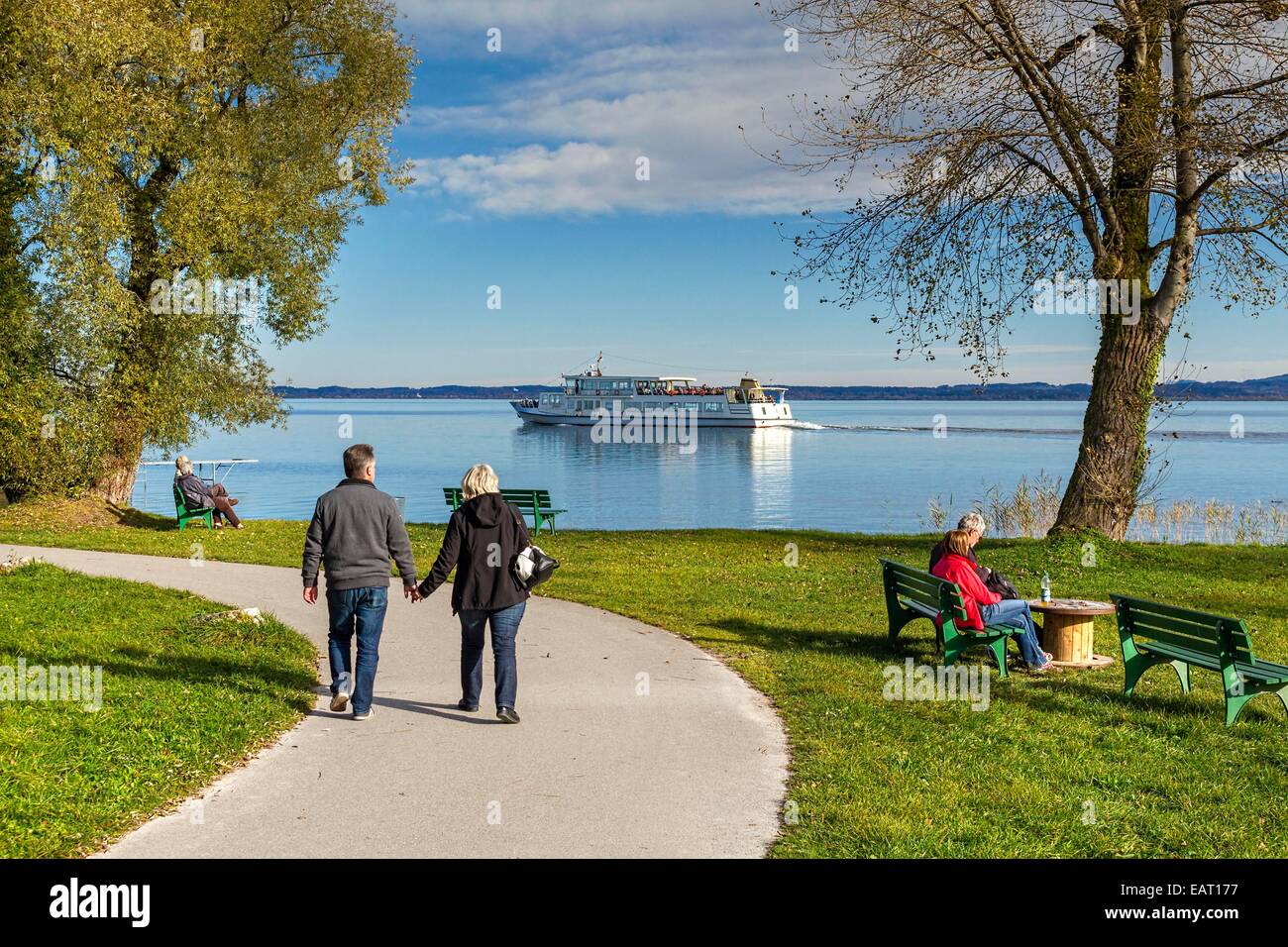 Couples walking and sitting on a park benches as a Chiemsee Ferry passes by, Fraueninsel ...