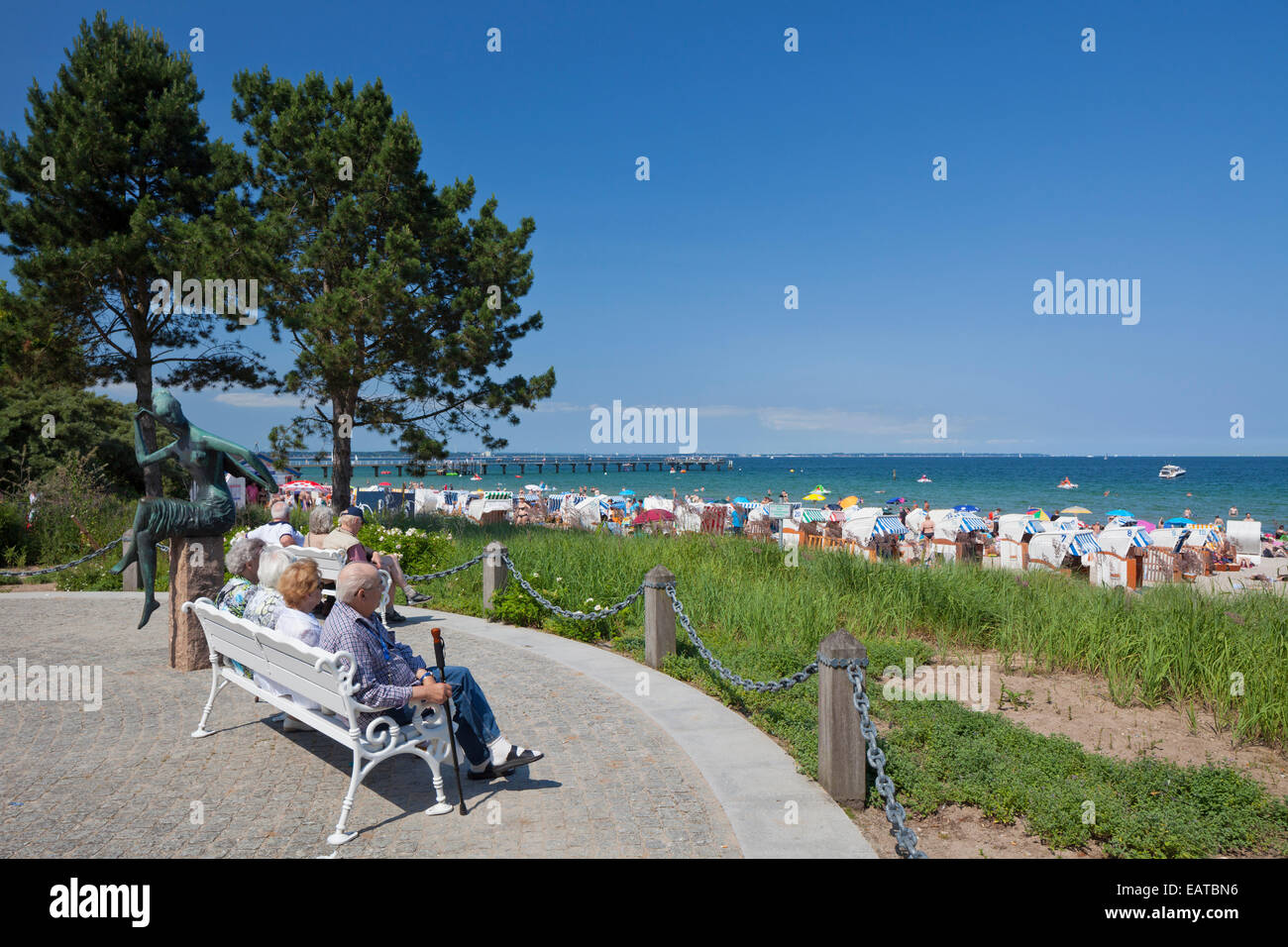 Tourists sitting on bench and looking over the beach at Timmendorfer ...
