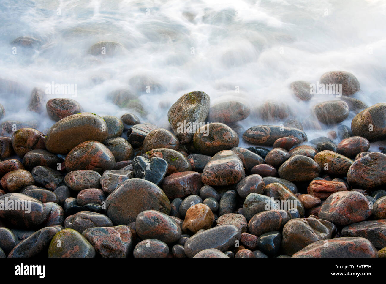 Close up of colourful cobbles covered by wave on shingle beach at ...