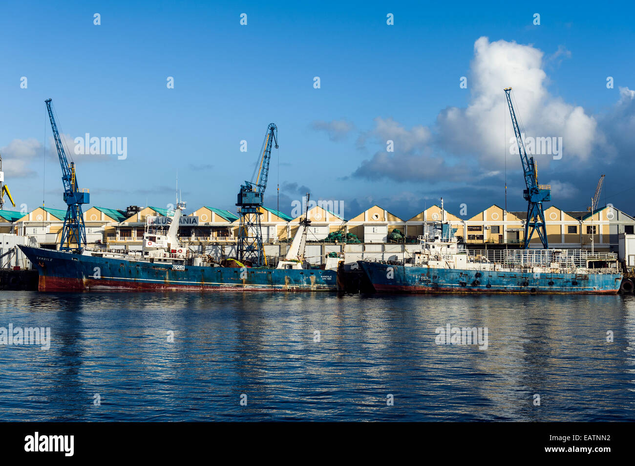 Rusting fishing boats anchored at a factory wharf lined with cranes ...