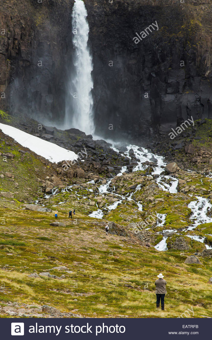 Distant hikers stand near a waterfall in a lush landscape Stock Photo ...