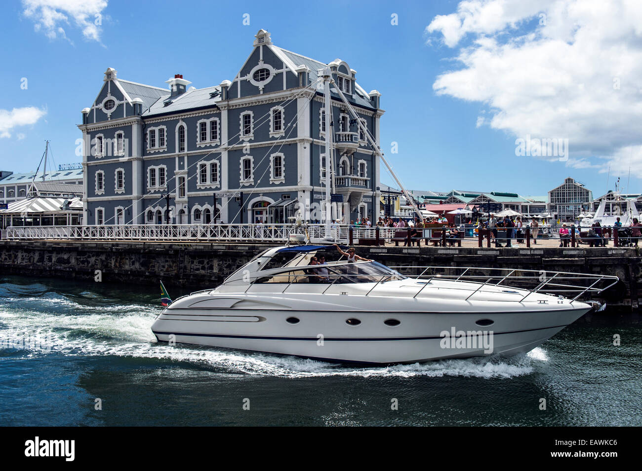 A luxury boat sails through a marina and docks crowded with tourists ...