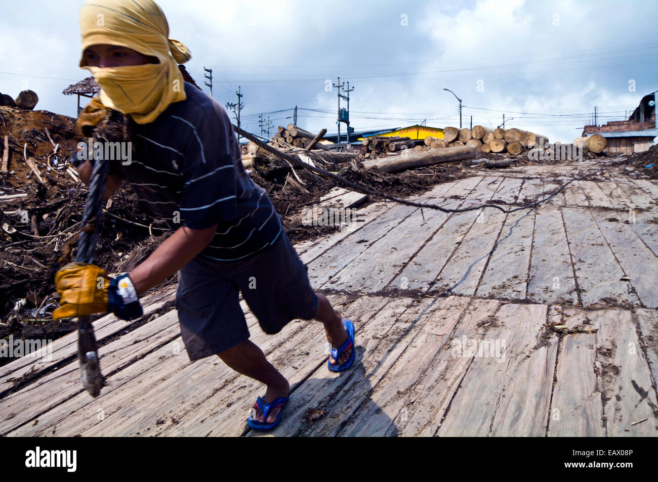 A logging mill laborer tows a heavy steel cable to a barge to collect ...