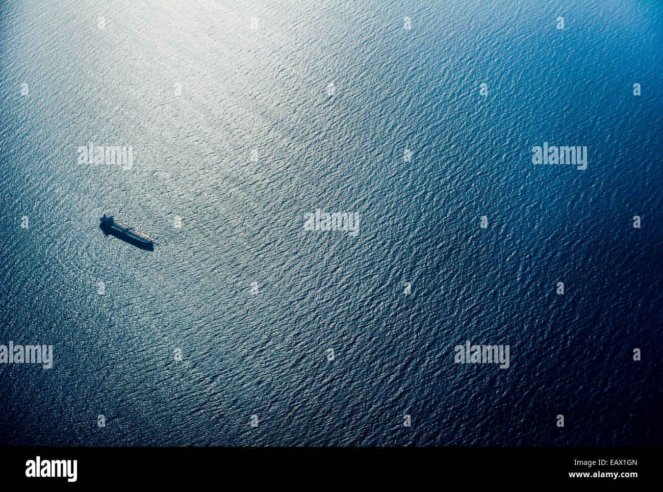 A cargo ship sailing across a vast blue ocean in the late afternoon ...