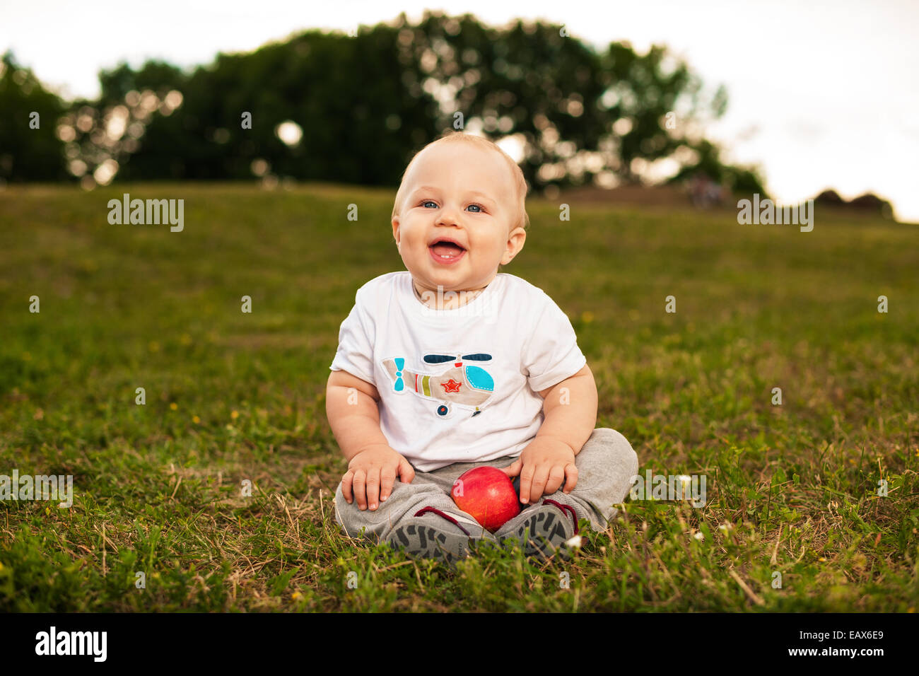 Smiling beautiful baby looking at camera and eating apple outdoors in ...