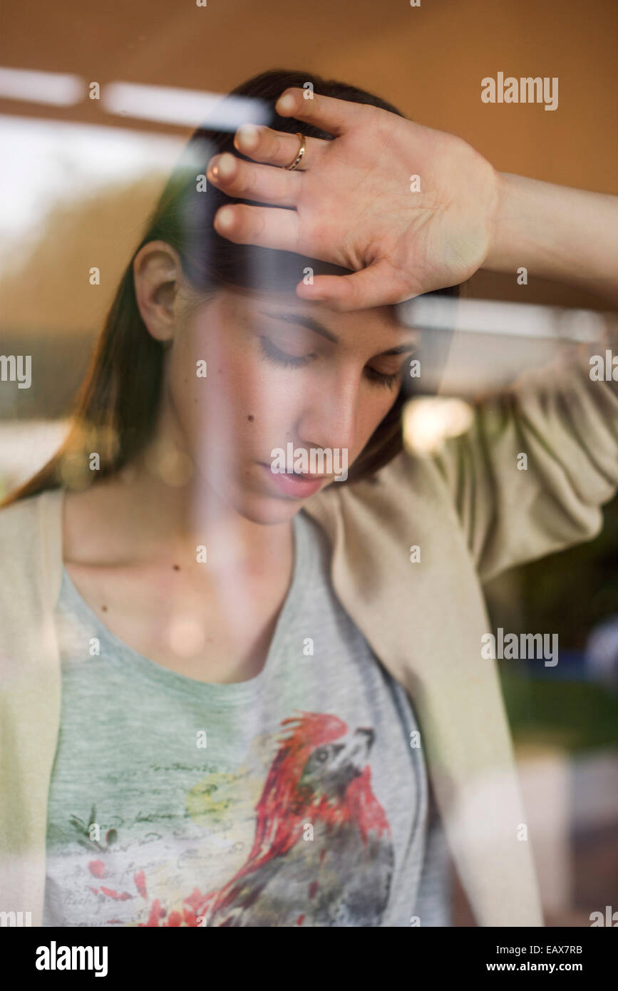 Woman leaning against window looking down with air of disappointment ...