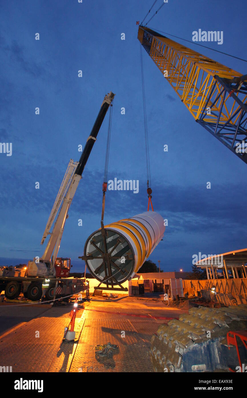 Construction job-site cranes lifting large tube structure at sunrise ...