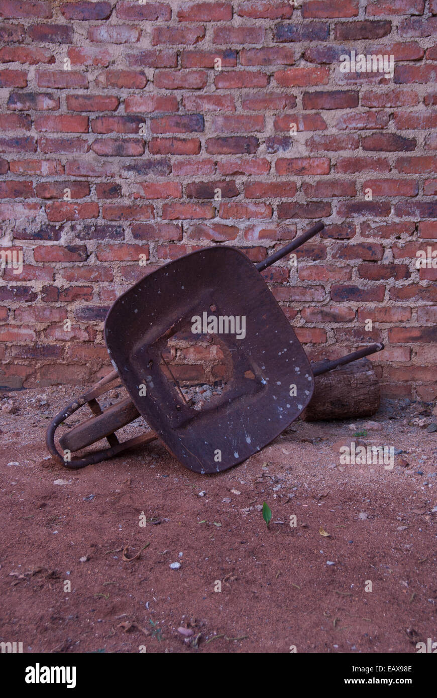 Old broken rusted wheelbarrow against a brick wall on a building site ...