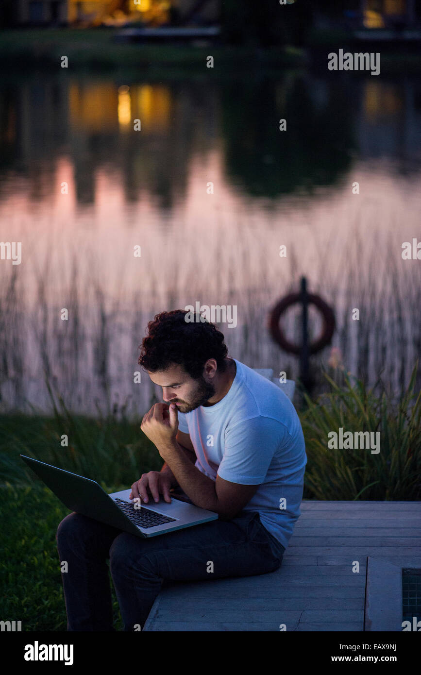 Man using laptop computer on lakeshore deck Stock Photo - Alamy