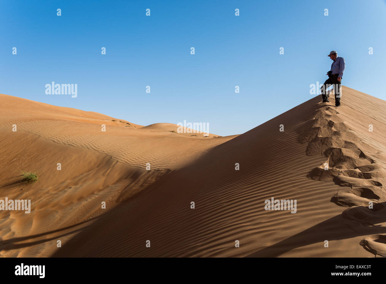 A man with a camera standing on top of a sand dune in the desert of ...