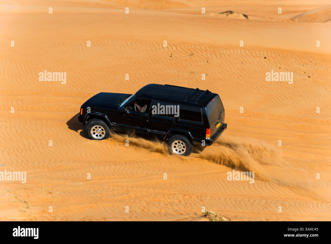 A four-wheel drive jeep driving over sand dunes in the desert of Oman ...