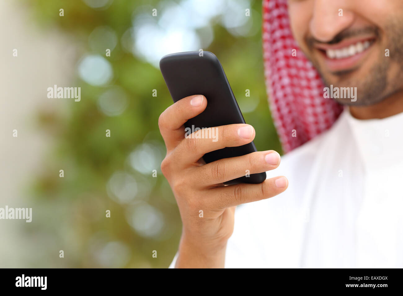 Smiling arab saudi man hand using a smart phone outdoor in a park with ...