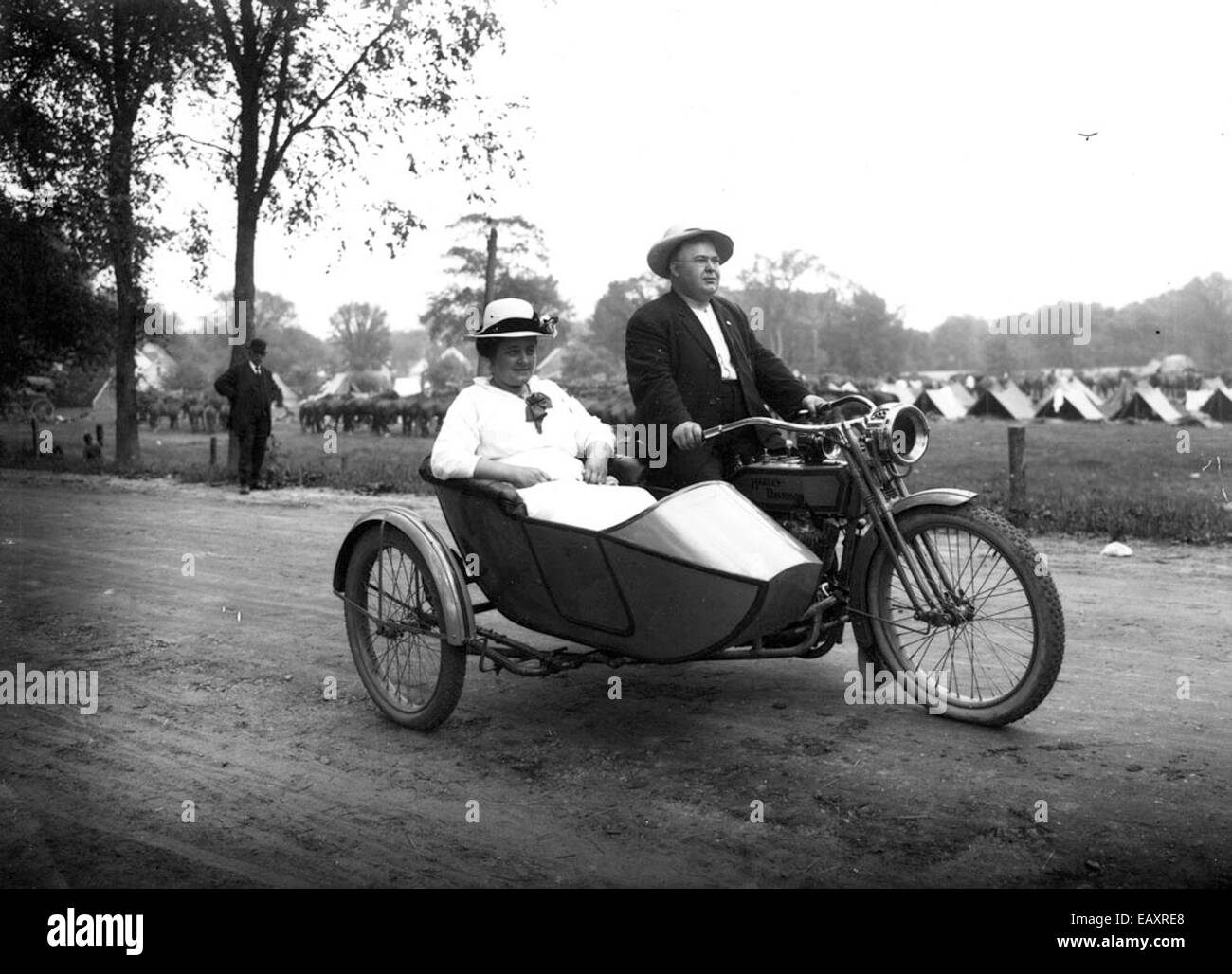 This photograph features a man riding an old-fashioned Harley Davidson ...