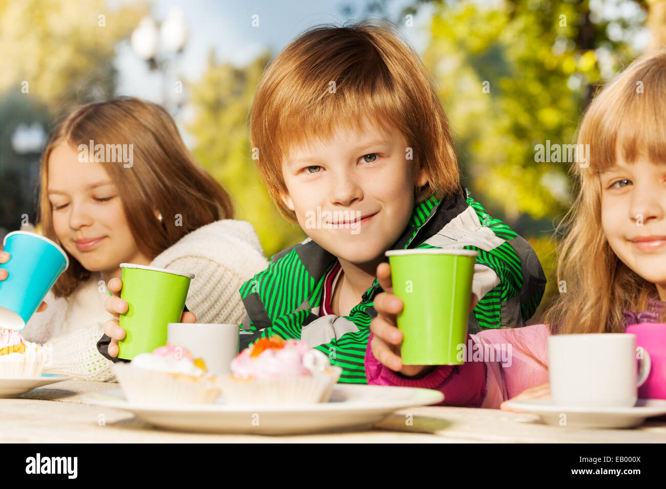 Smiling kids with tea cups sitting outside Stock Photo - Alamy