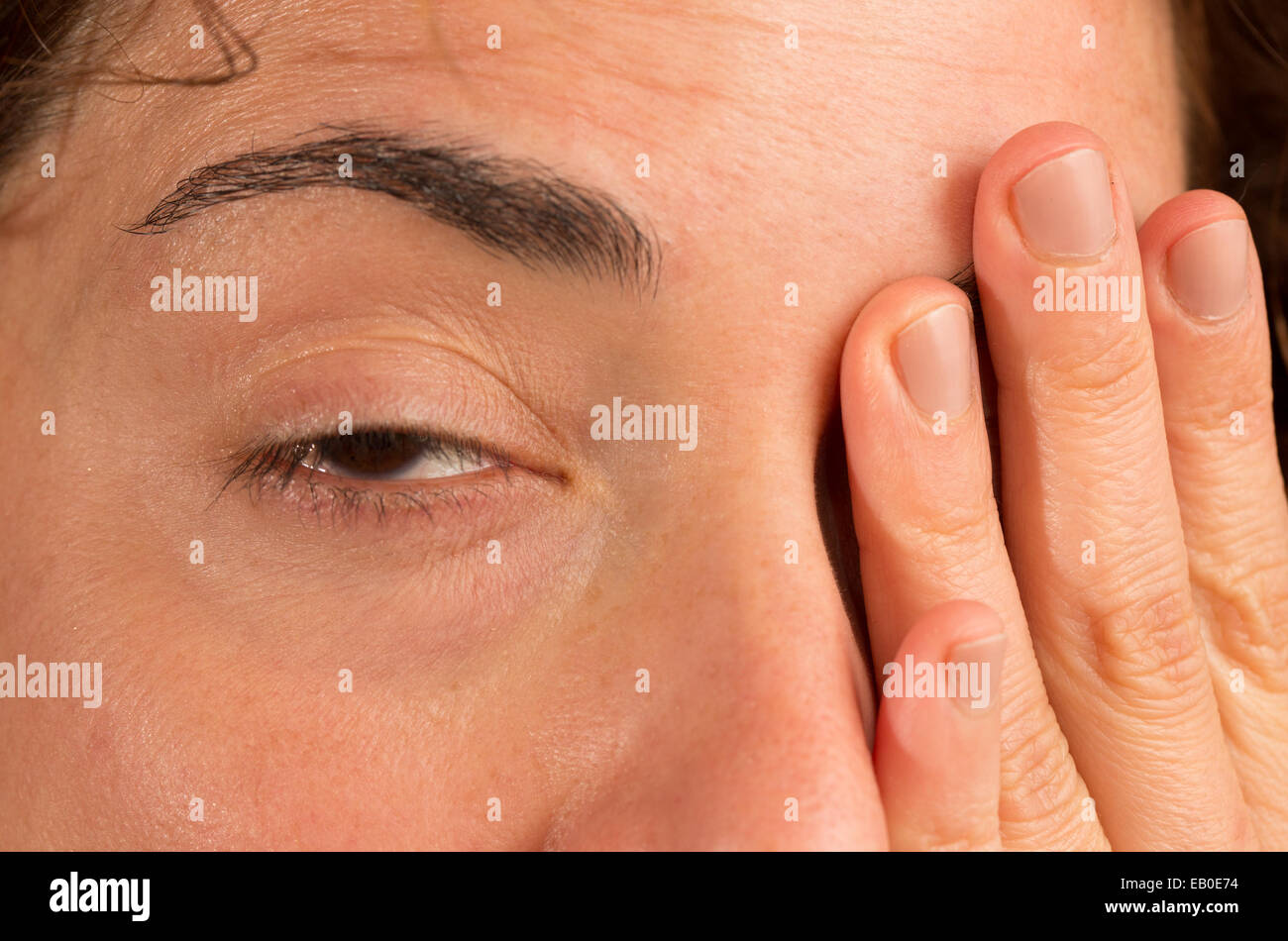 Caucasian woman with right eye almost closd and hand over left one ...