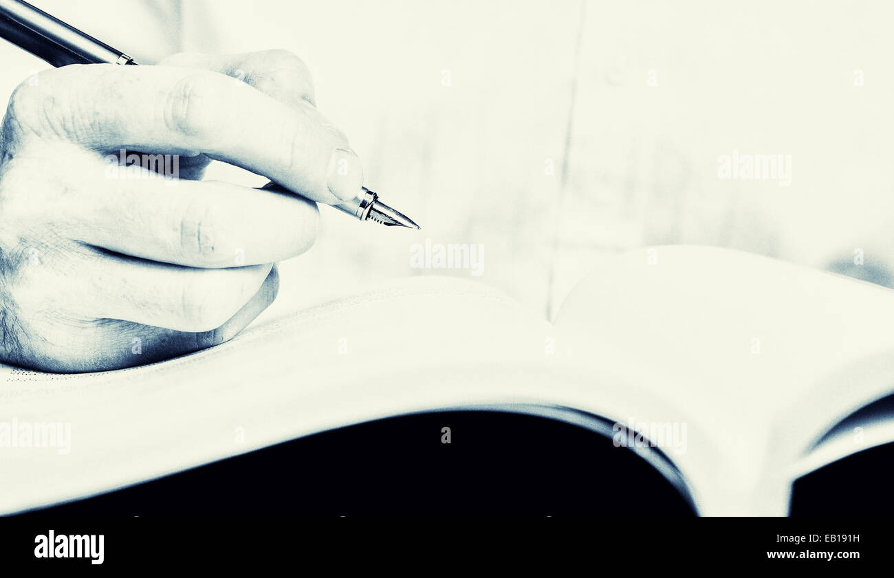 A hand holding a fountain pen and about to writer a note or highlight ...