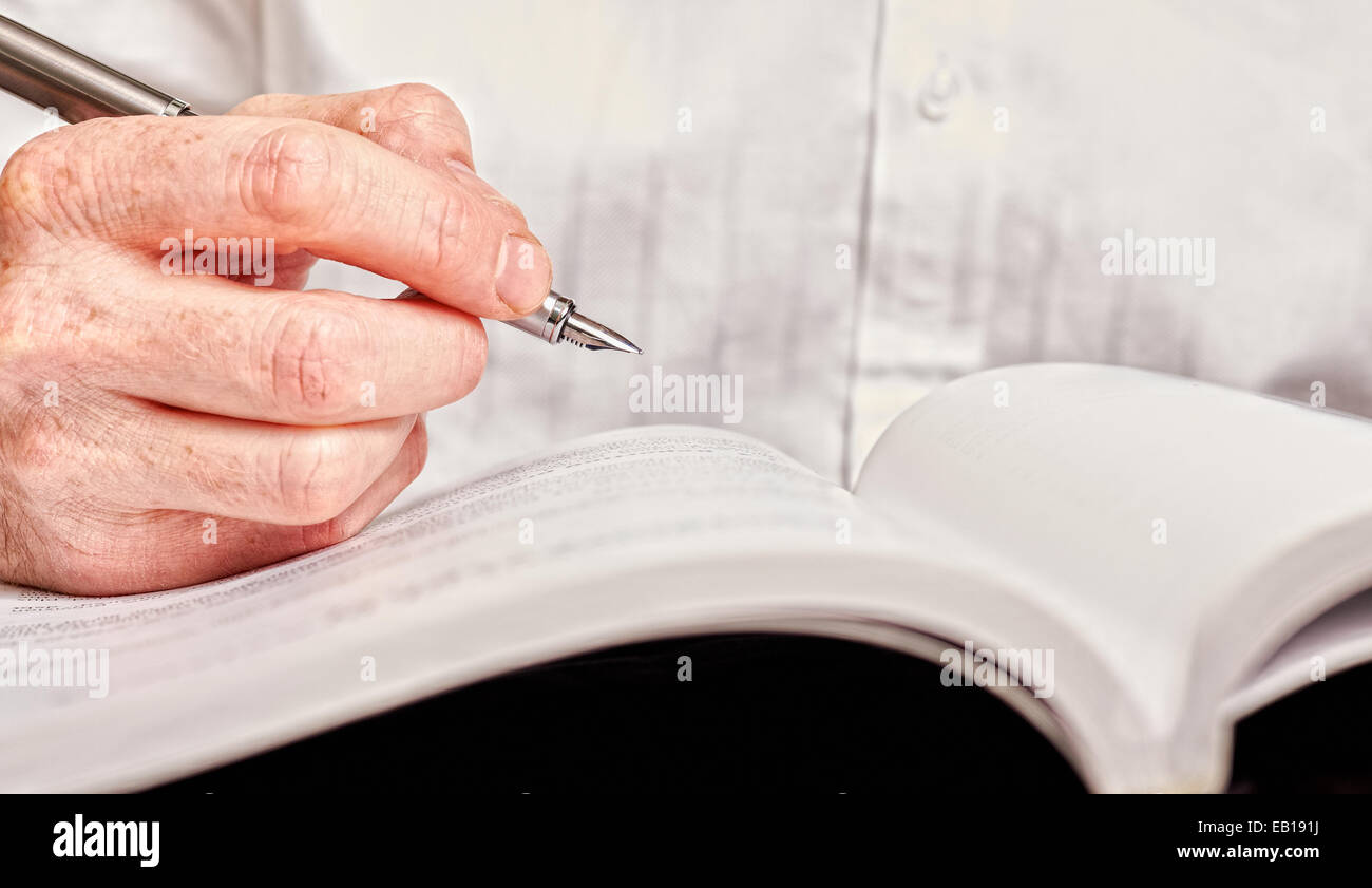A hand holding a fountain pen and about to writer a note or highlight ...