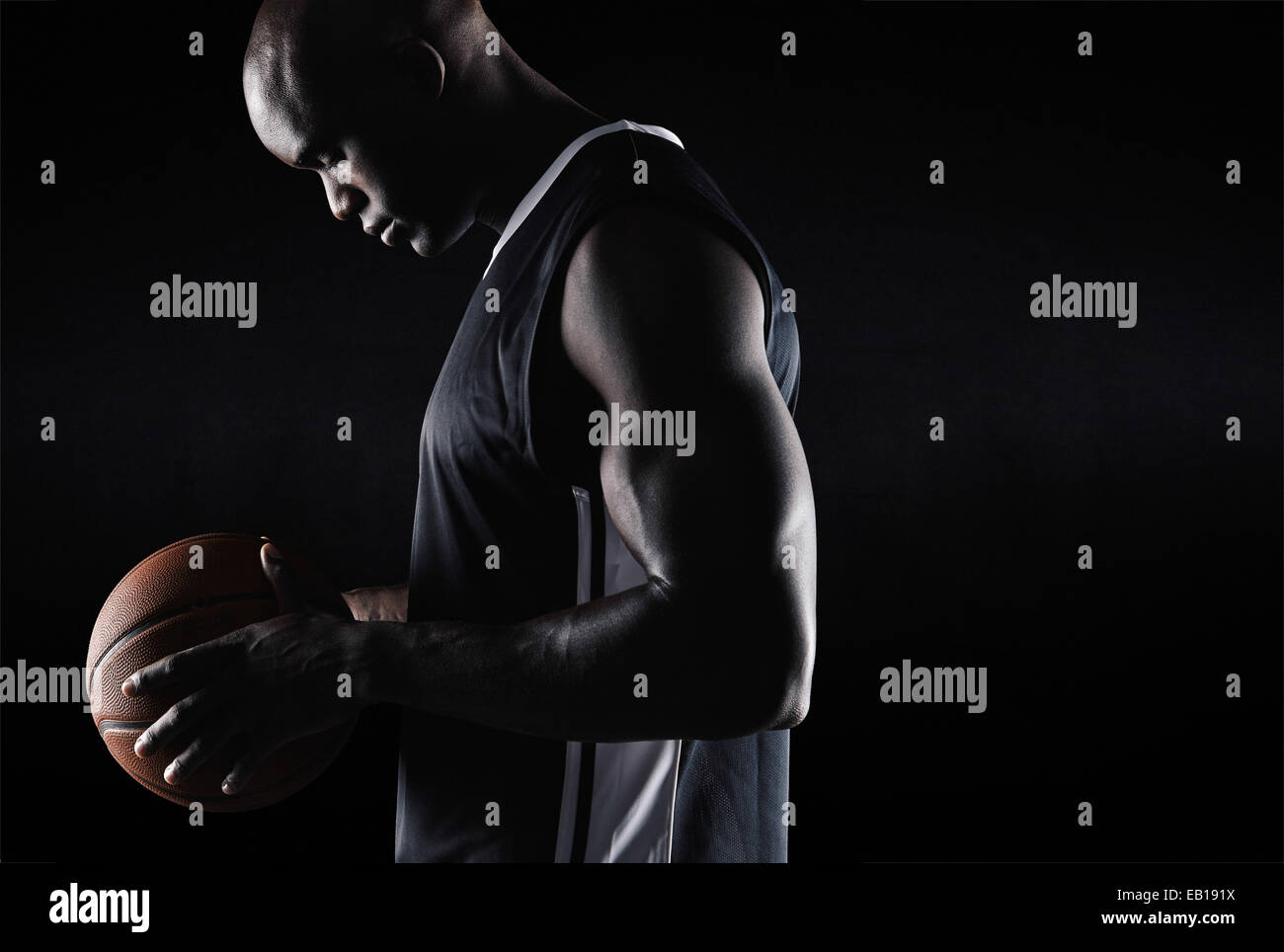 Side view of fit young basketball player holding ball against black ...