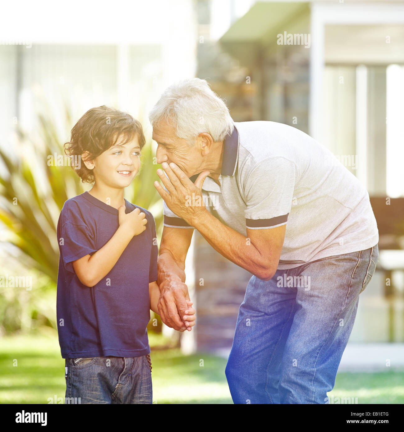 Grandfather whispering a secret in the ear of his grandson in a garden ...