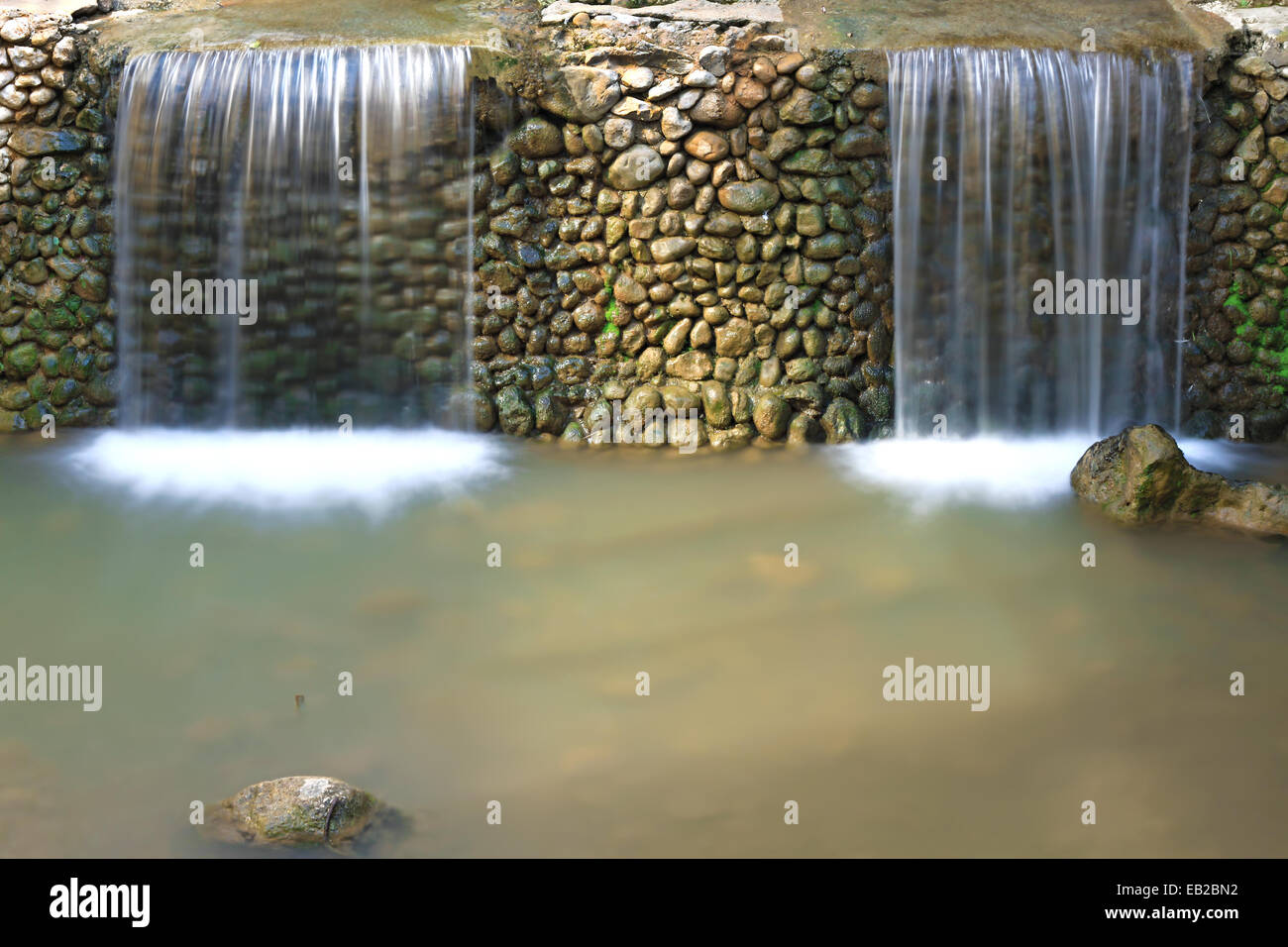 Two small waterfalls separated by a stone wall Stock Photo - Alamy