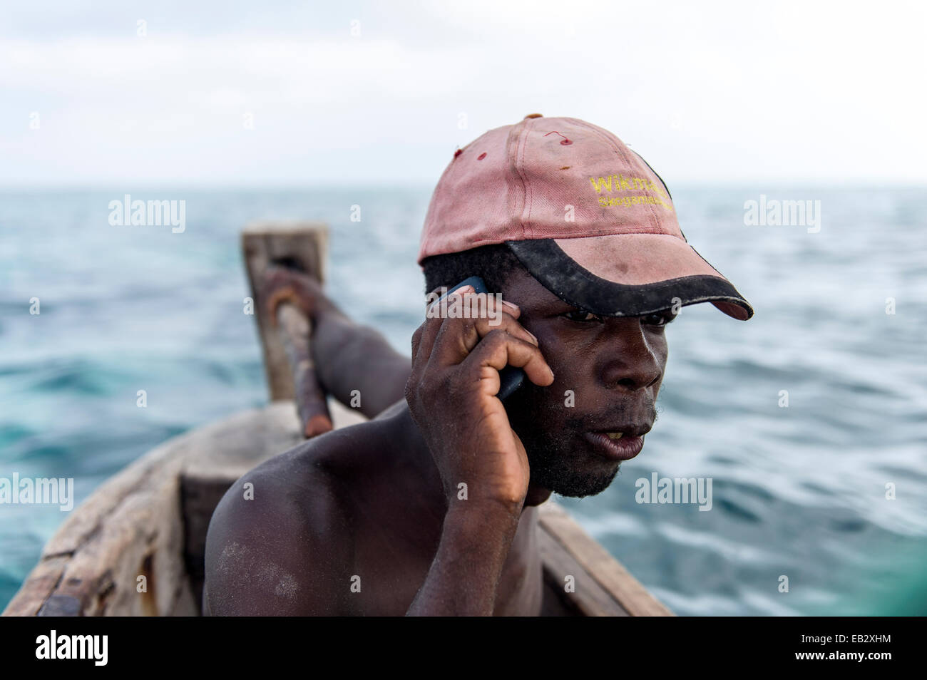 A fisherman on his mobile phone, steers his wooden trimaran sailing ...