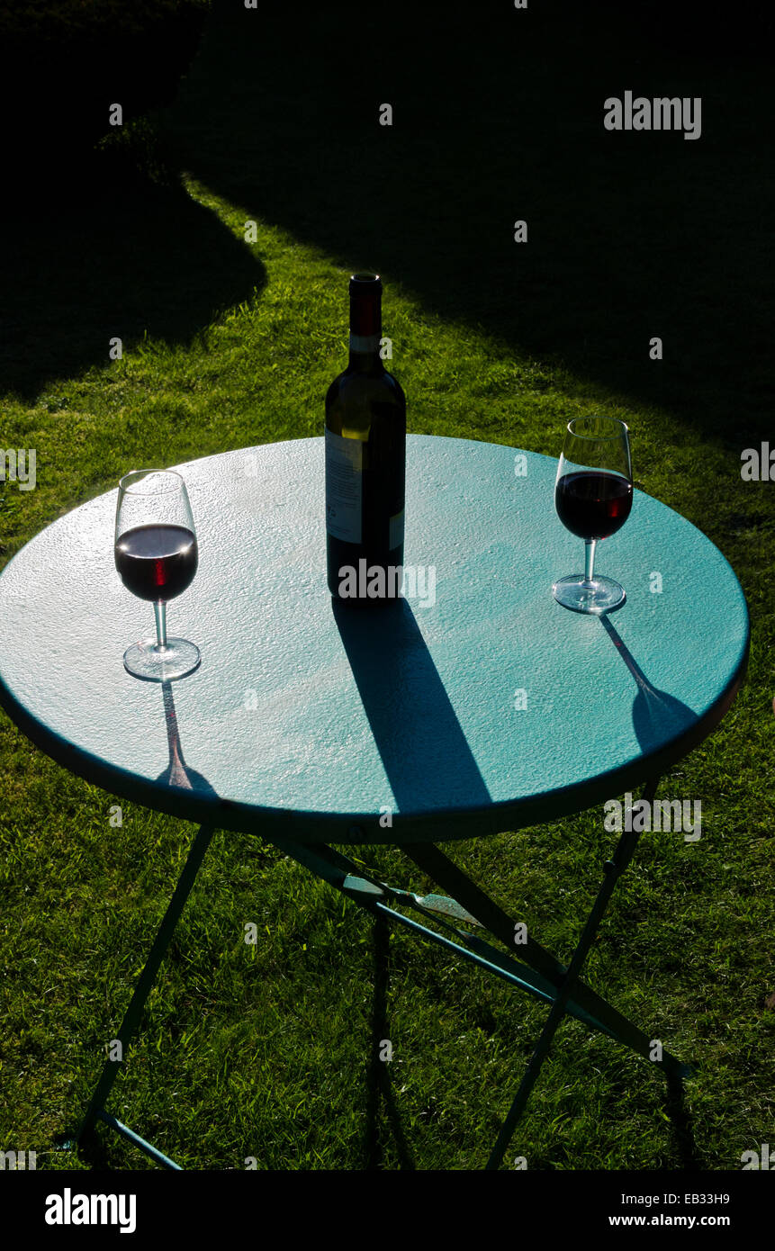 Al-fresco drinking red wine bottle and two filled glasses with garden ...